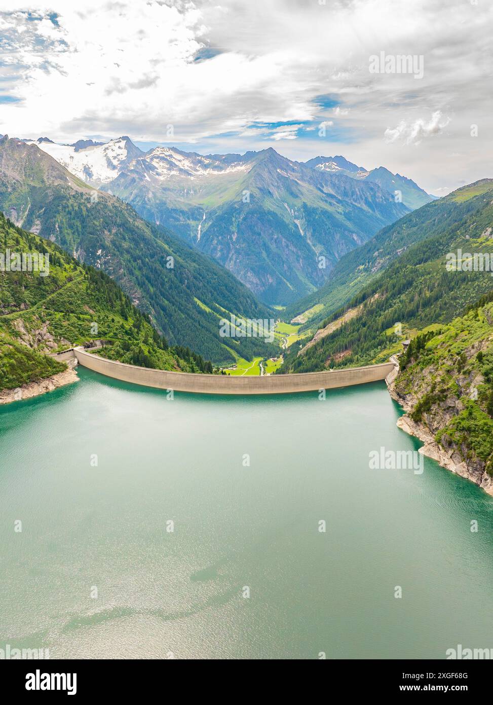 A large reservoir with a dam, surrounded by high mountains and green ...