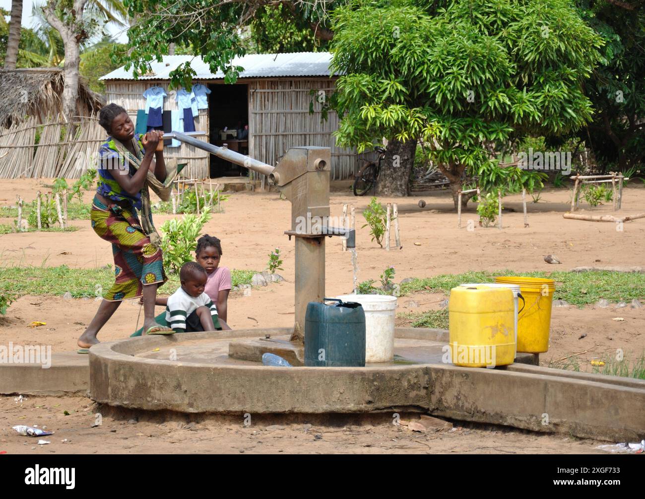 Clean water pump, Licaca, Inhambane, Mozambique. Woman pumping clean water while her chidlren ...