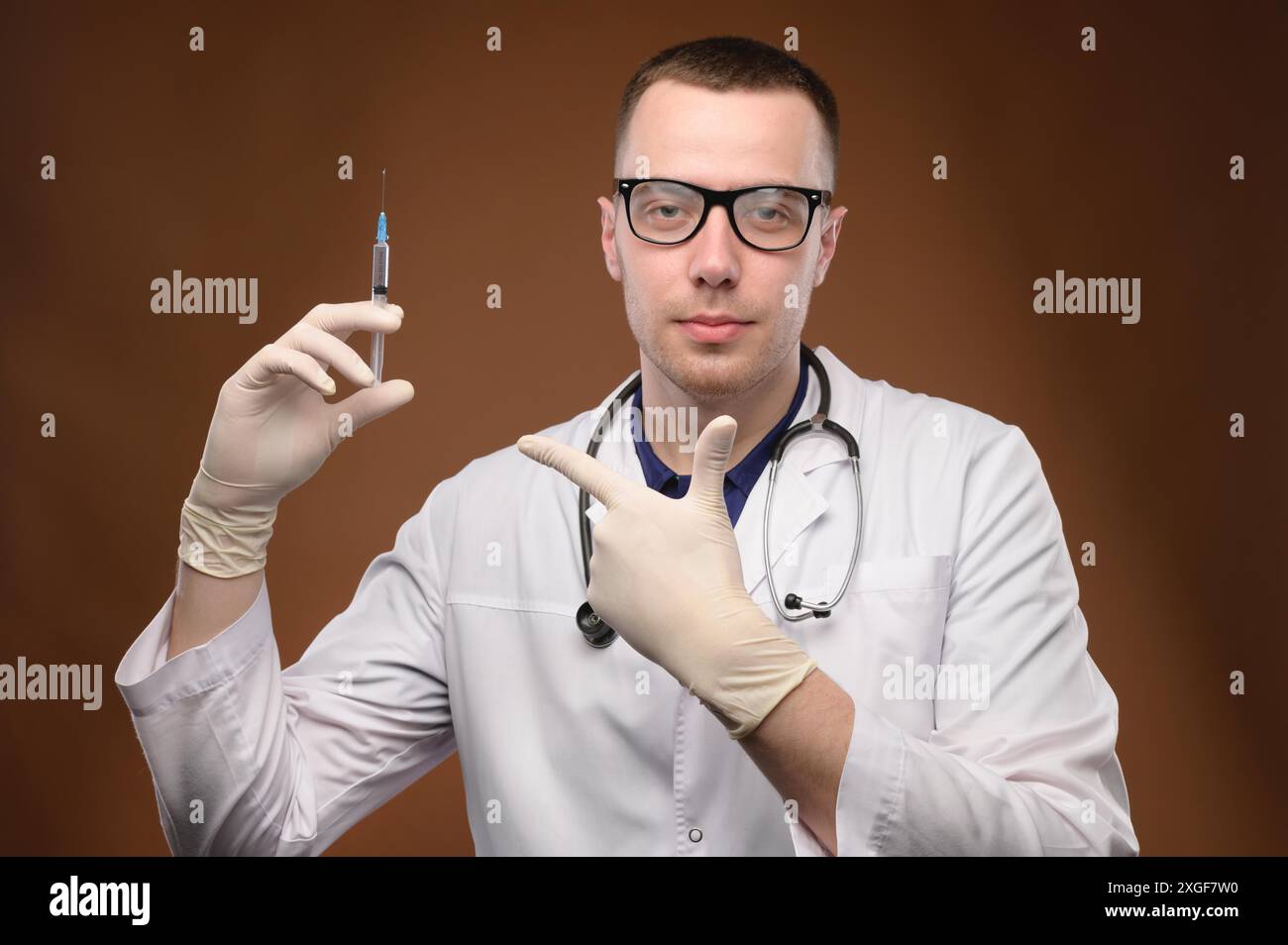 A young Caucasian doctor in a white coat and glasses holds a syringe ...