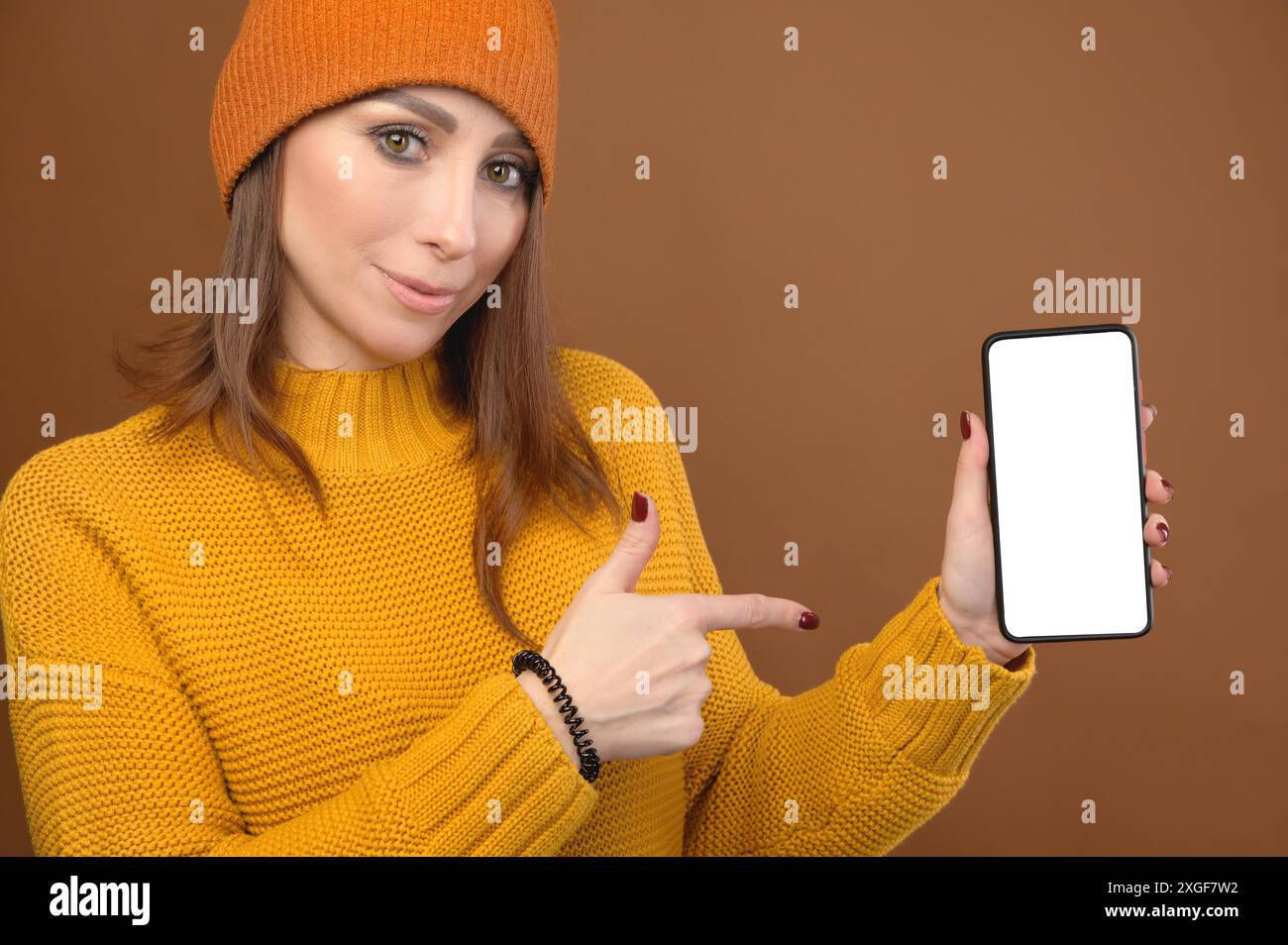 Smiling caucasian young lady pointing with finger at smartphone in hand ...