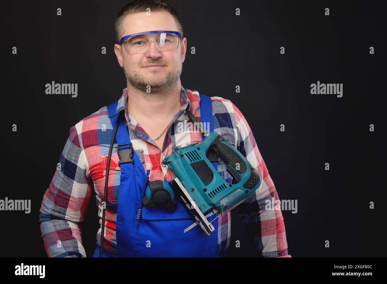 A male builder in goggles and a uniform on a black background smiles, a ...