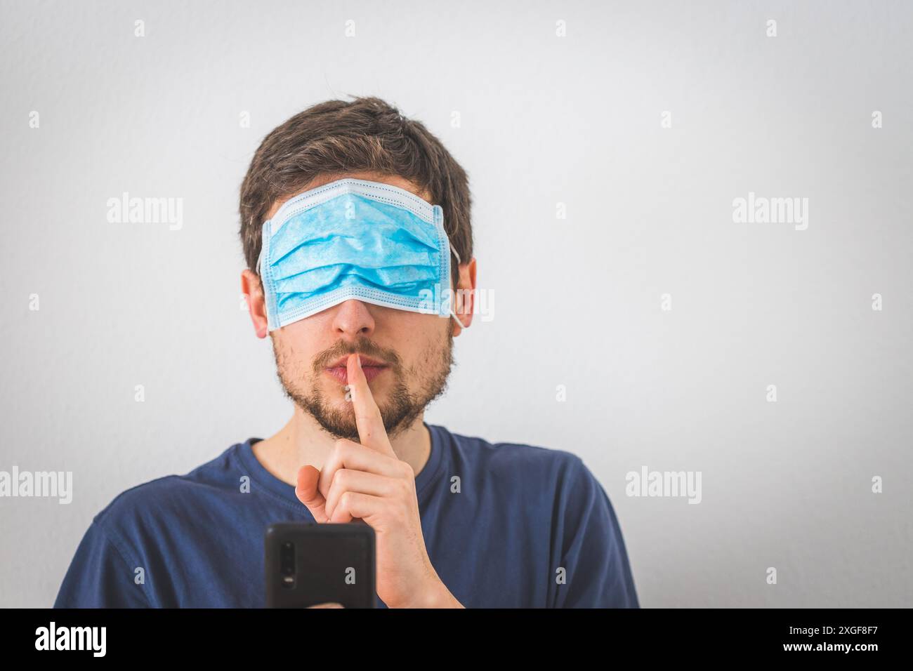 Young angry man with face mask over the eyes is doing a psst! gesture ...