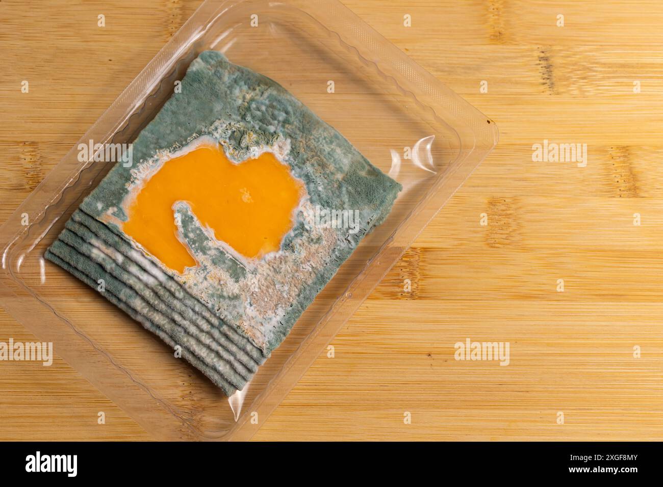 Slices of moldy yellow cheese arranged on a bamboo cutting board. Green ...