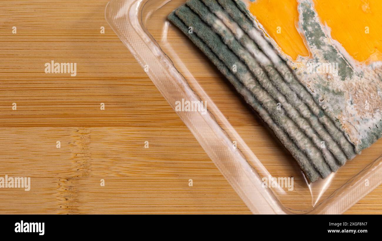 Slices of moldy yellow cheese arranged on a bamboo cutting board. Green ...