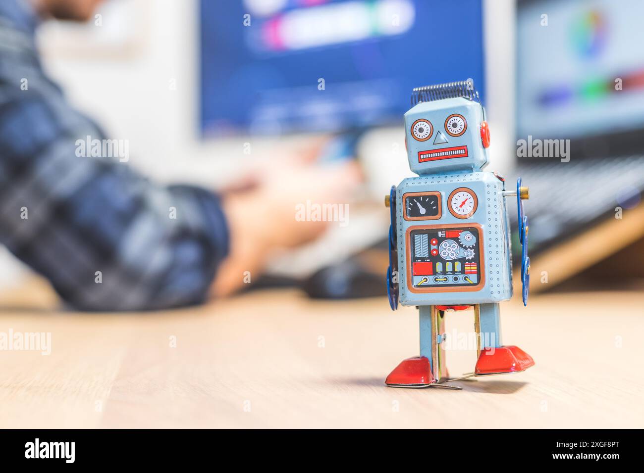 Toy robot on a desktop, man working on the computer in the background ...