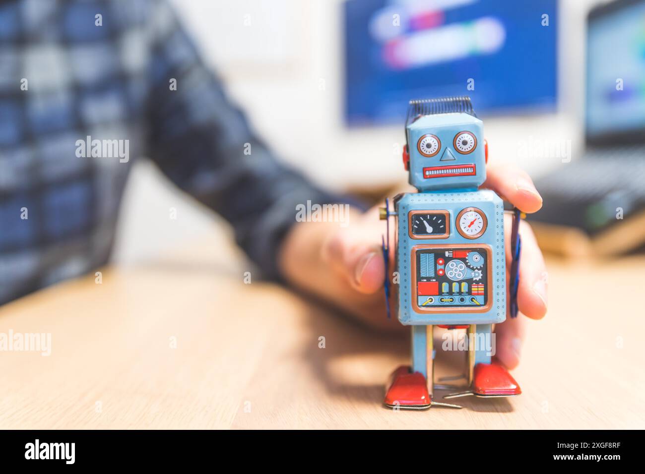 Toy robot on a desktop, man working on the computer in the background ...