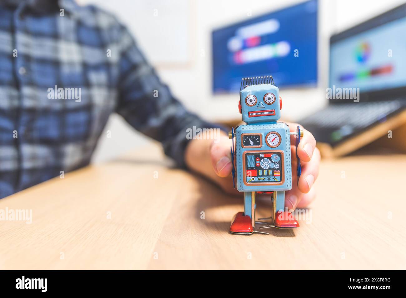 Toy robot on a desktop, man working on the computer in the background ...