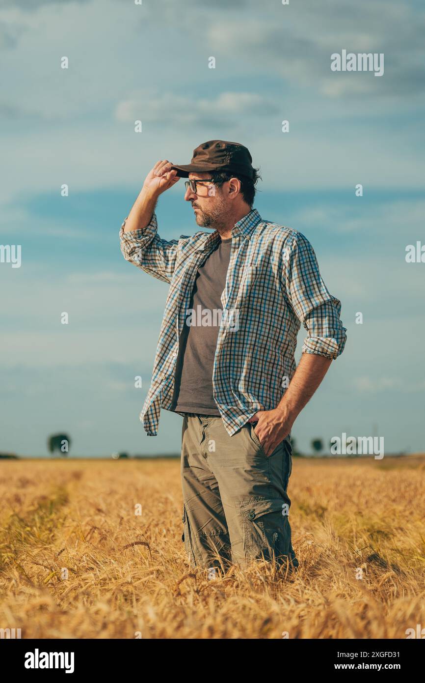 Male farmer standing in ripe wheat field and looking over the harvest ...