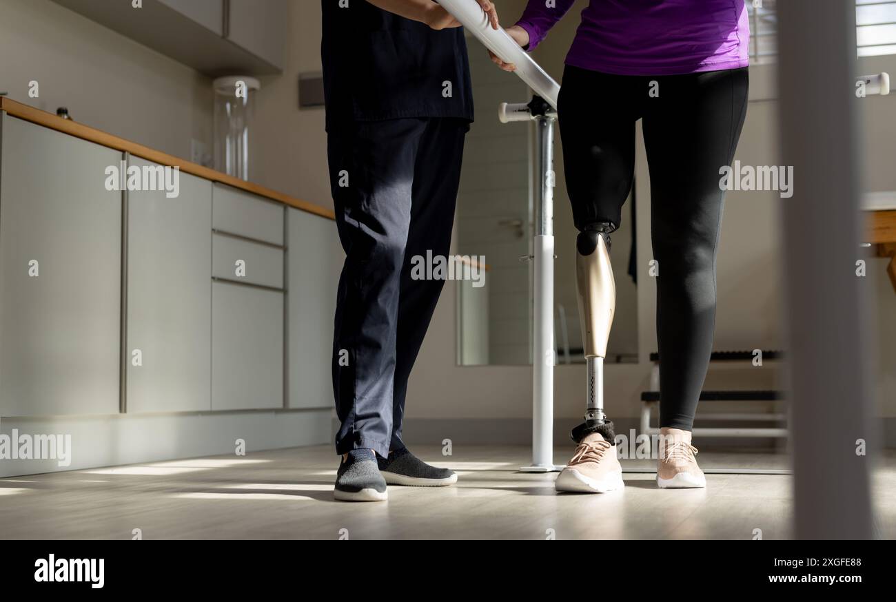 Walking with prosthetic leg, woman receiving assistance from therapist ...