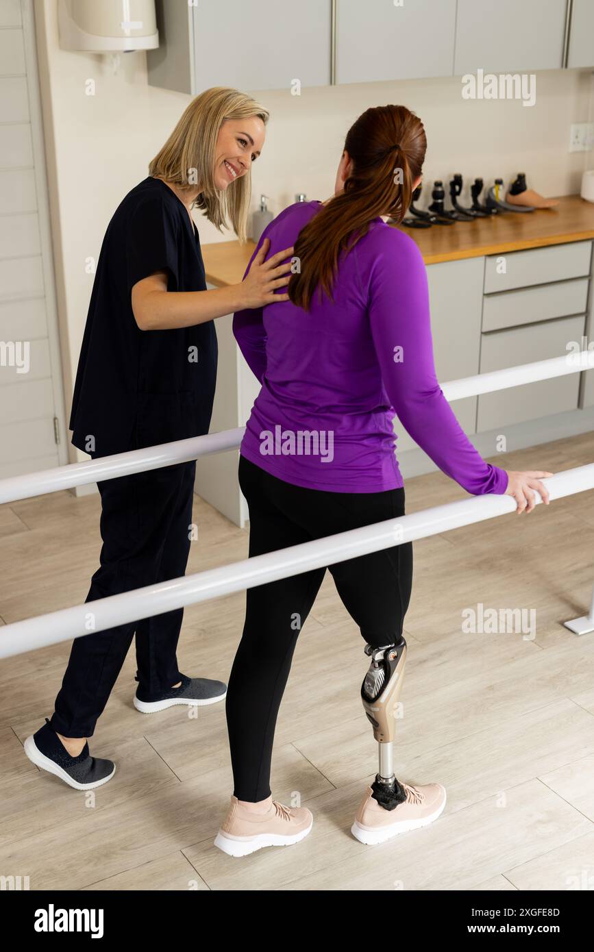 Walking with prosthetic leg, woman receiving support from therapist in ...