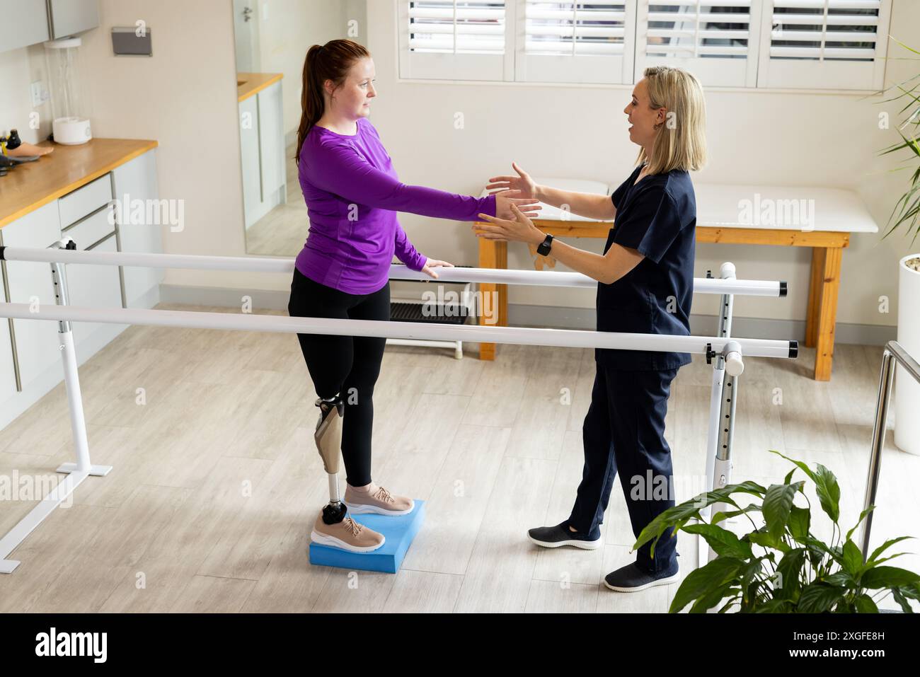 Woman with prosthetic leg balancing on foam pad, assisted by therapist ...