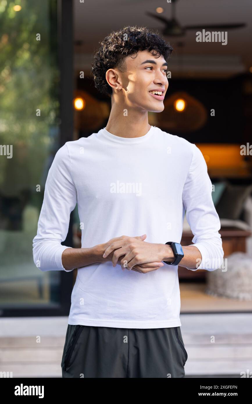 Wearing smartwatch, smiling young man standing outside modern home ...
