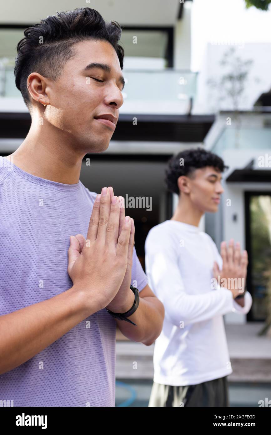 Practicing yoga, two men meditating with hands in prayer position ...