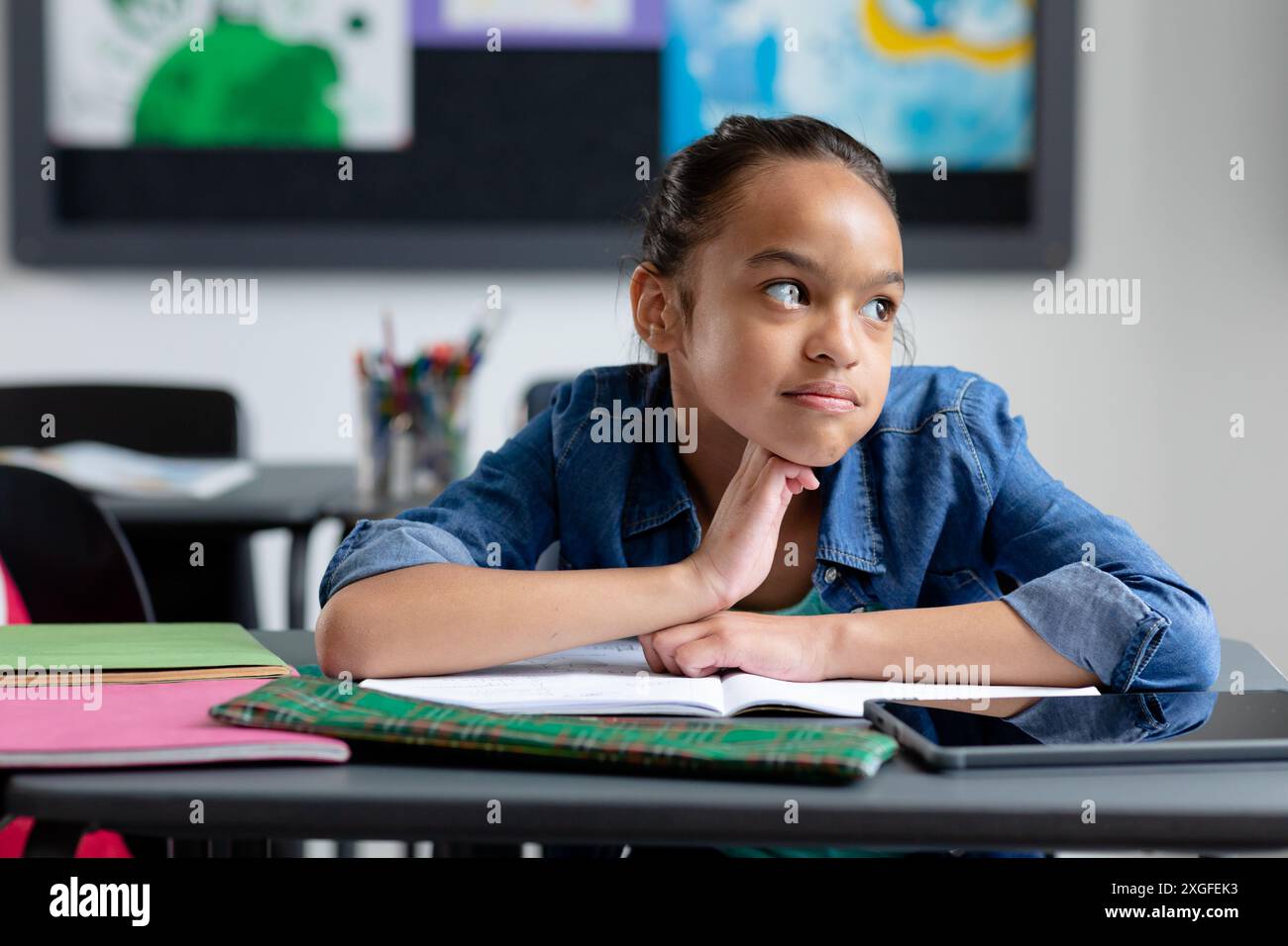 Bored biracial schoolgirl sitting at desk in class, leaning on hand ...