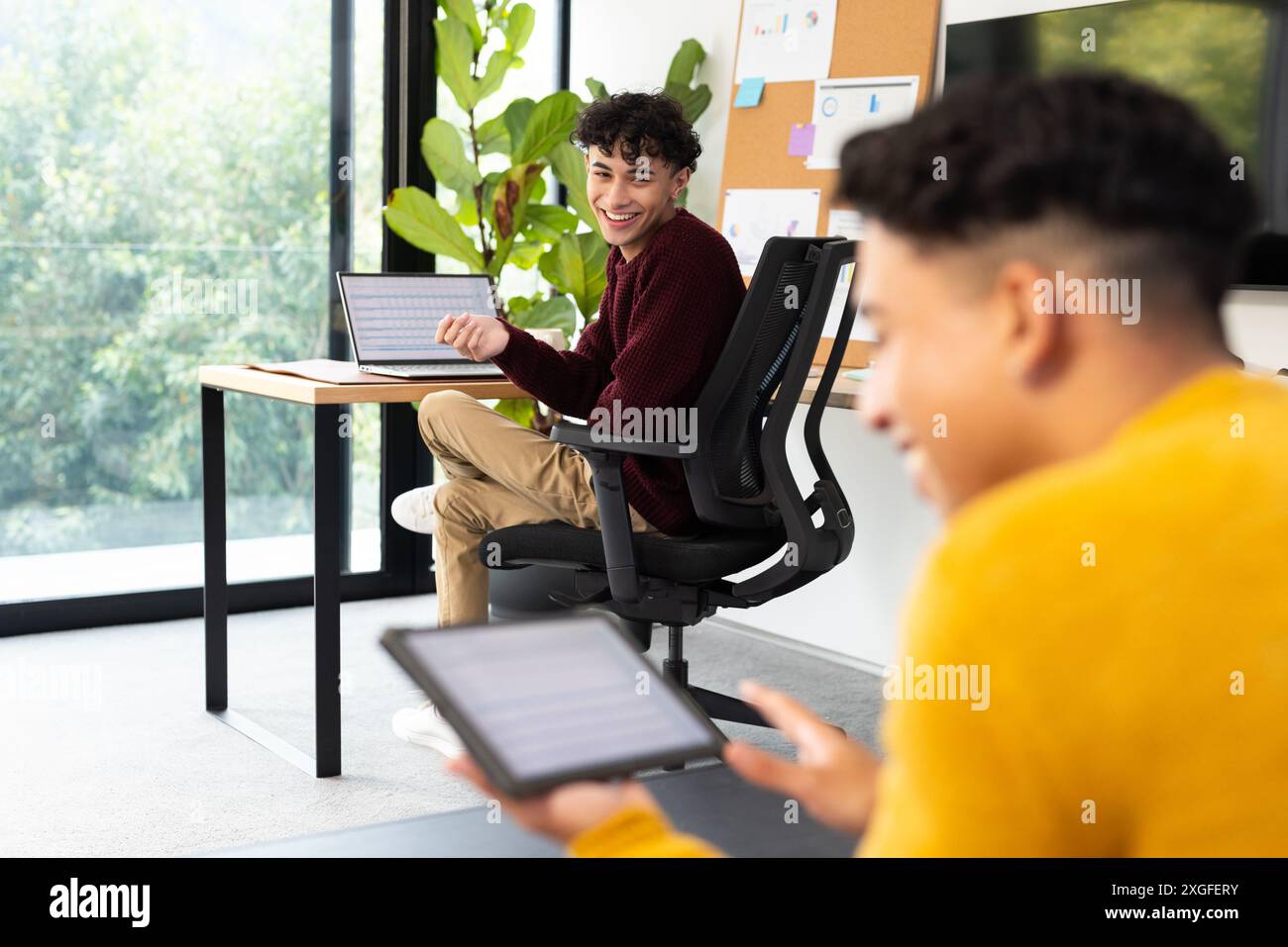 Using tablets and laptops, two men working and smiling in home office ...