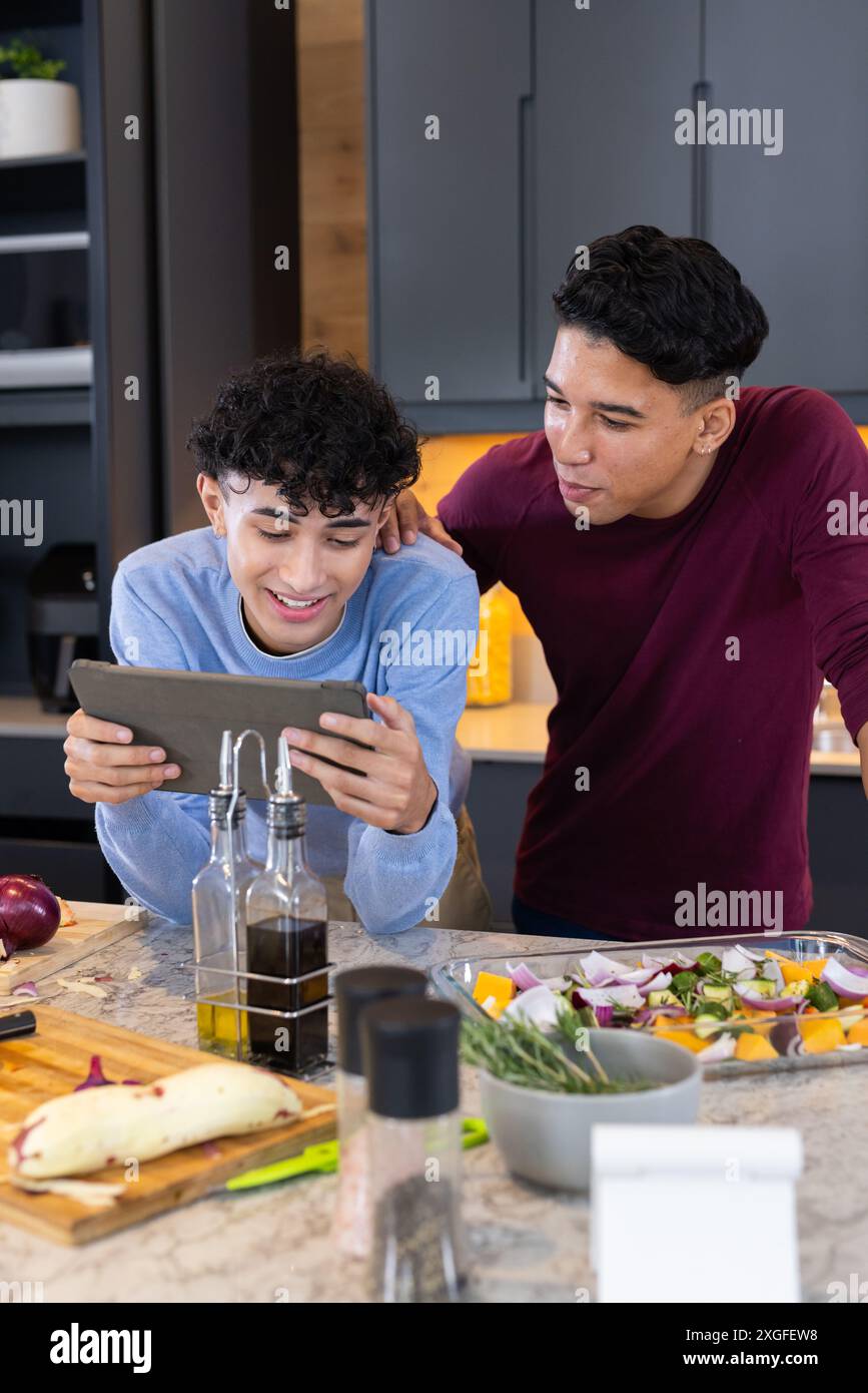 Cooking together, male gay couple using tablet for recipe in modern ...