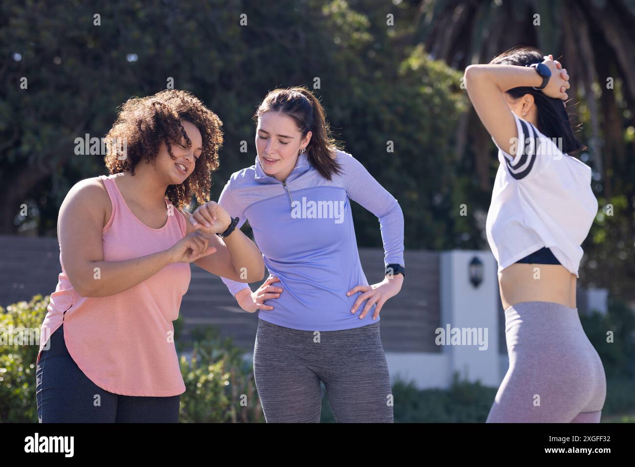 Exercising outdoors in activewear, three women friends checking fitness ...