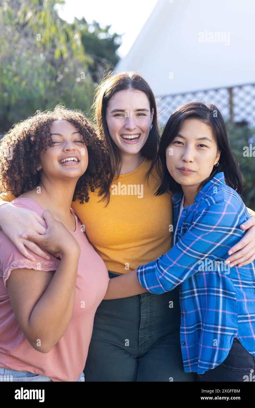 Hugging and smiling, three diverse women friends outdoors enjoying ...