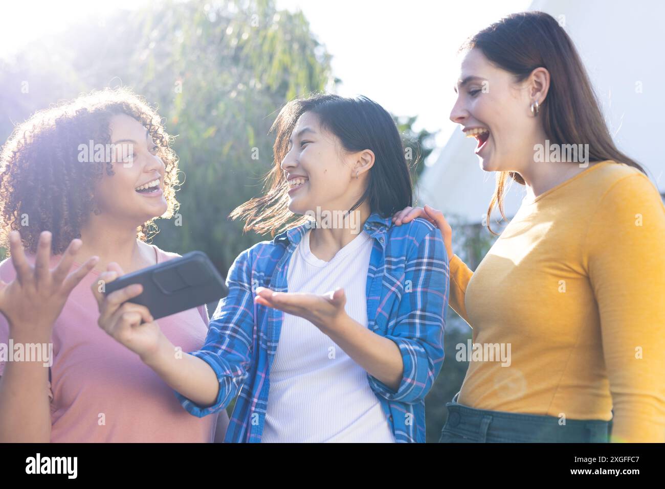 Smiling friends outdoors, holding smartphone and sharing exciting news ...