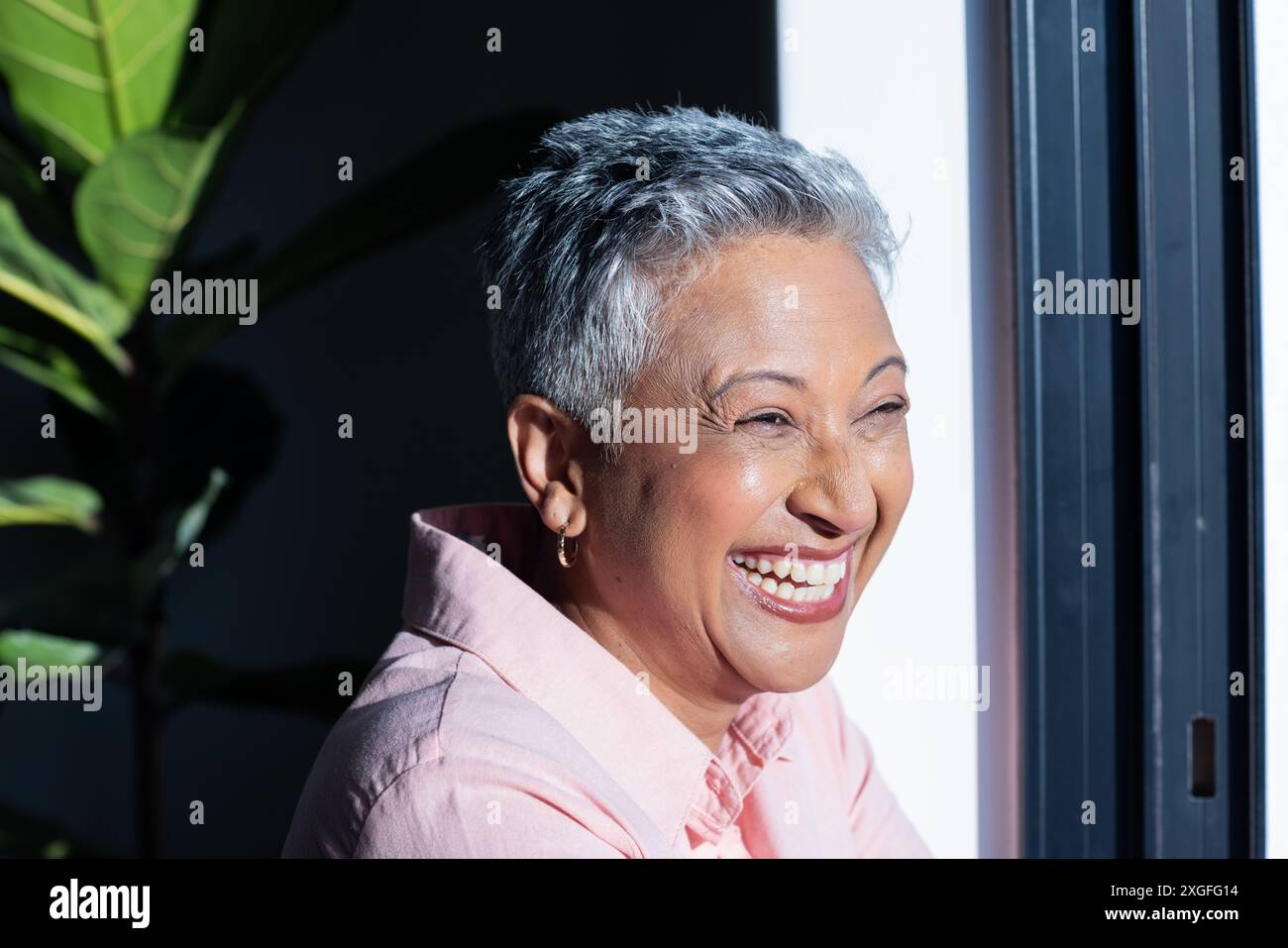 Smiling senior woman enjoying sunlight by window, feeling happy and ...