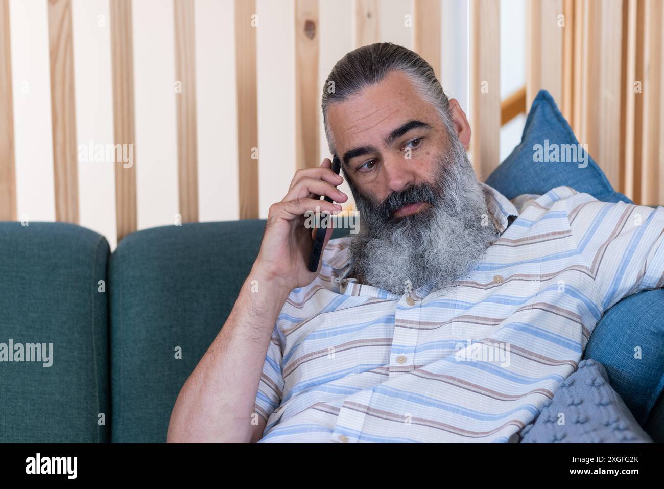 Talking on smartphone, senior man with beard sitting on couch indoors ...