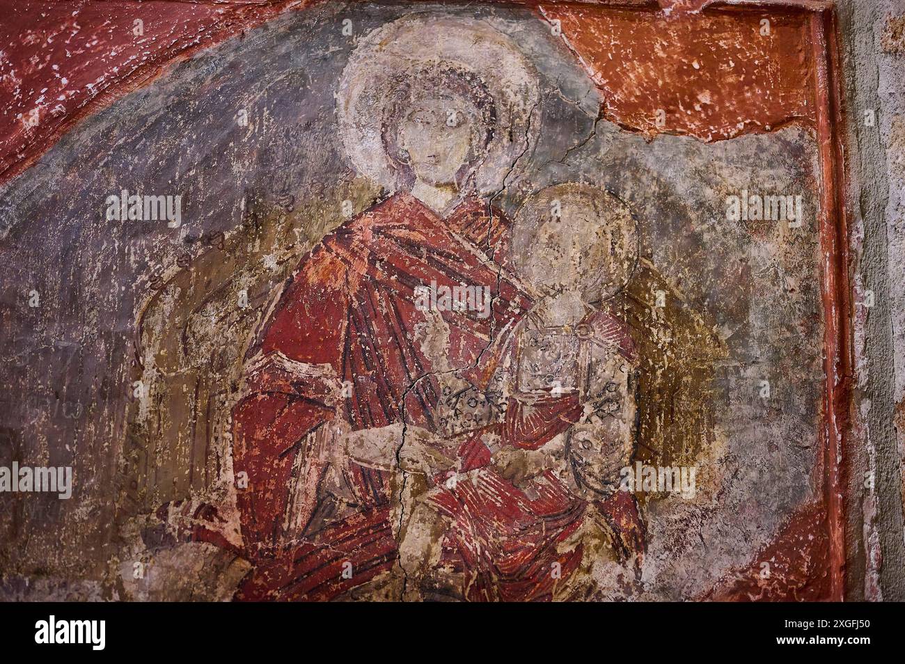 An old fresco shows a holy figure in red robes holding a child, with a ...