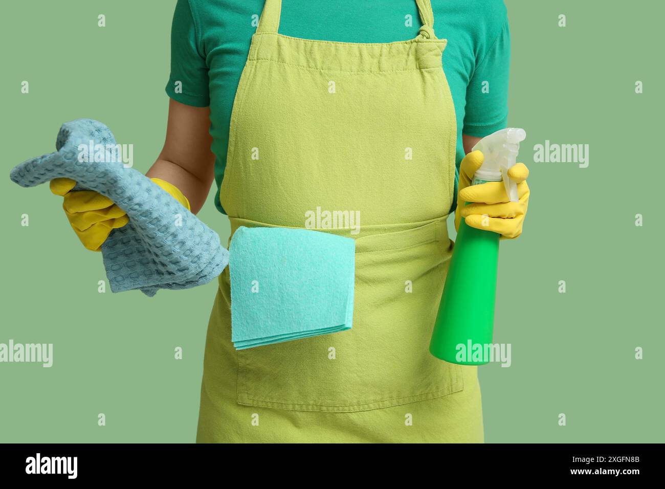 Woman in apron with spray bottle and rag on green background, closeup ...