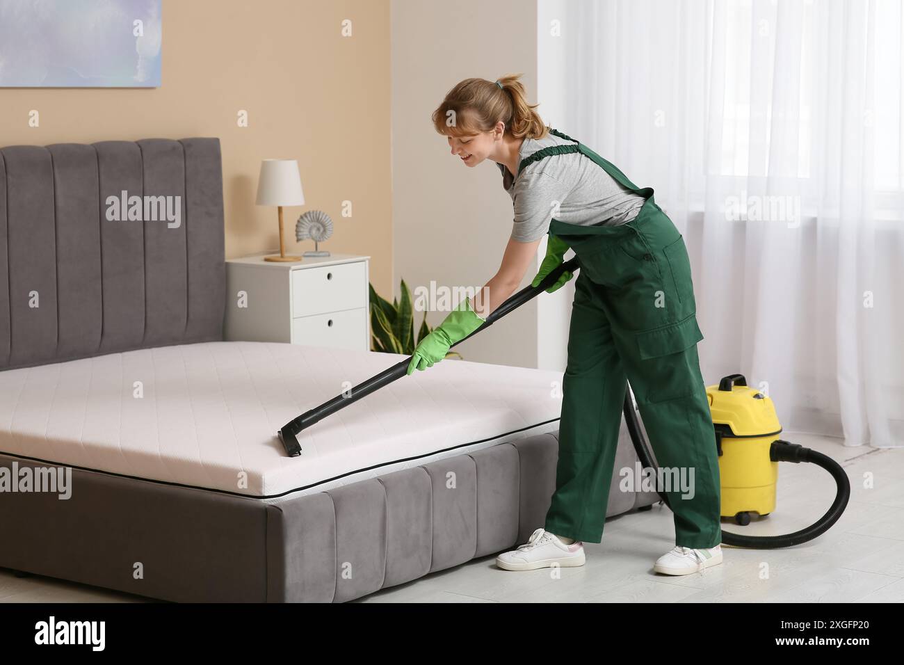 Female janitor cleaning mattress with vacuum cleaner in bedroom Stock ...