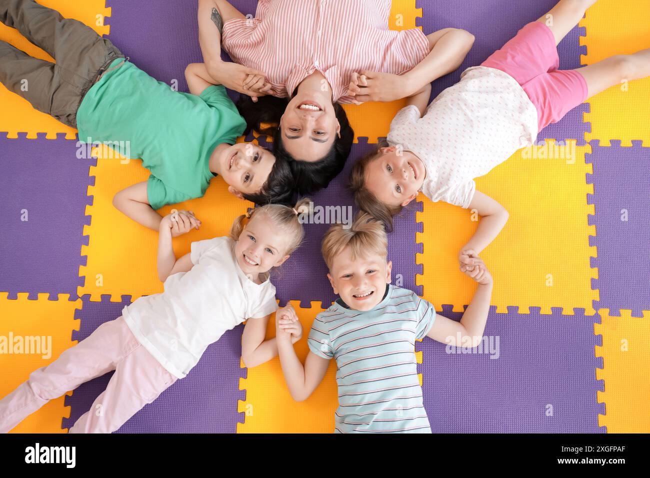 Little children with nursery teacher lying on floor in kindergarten ...