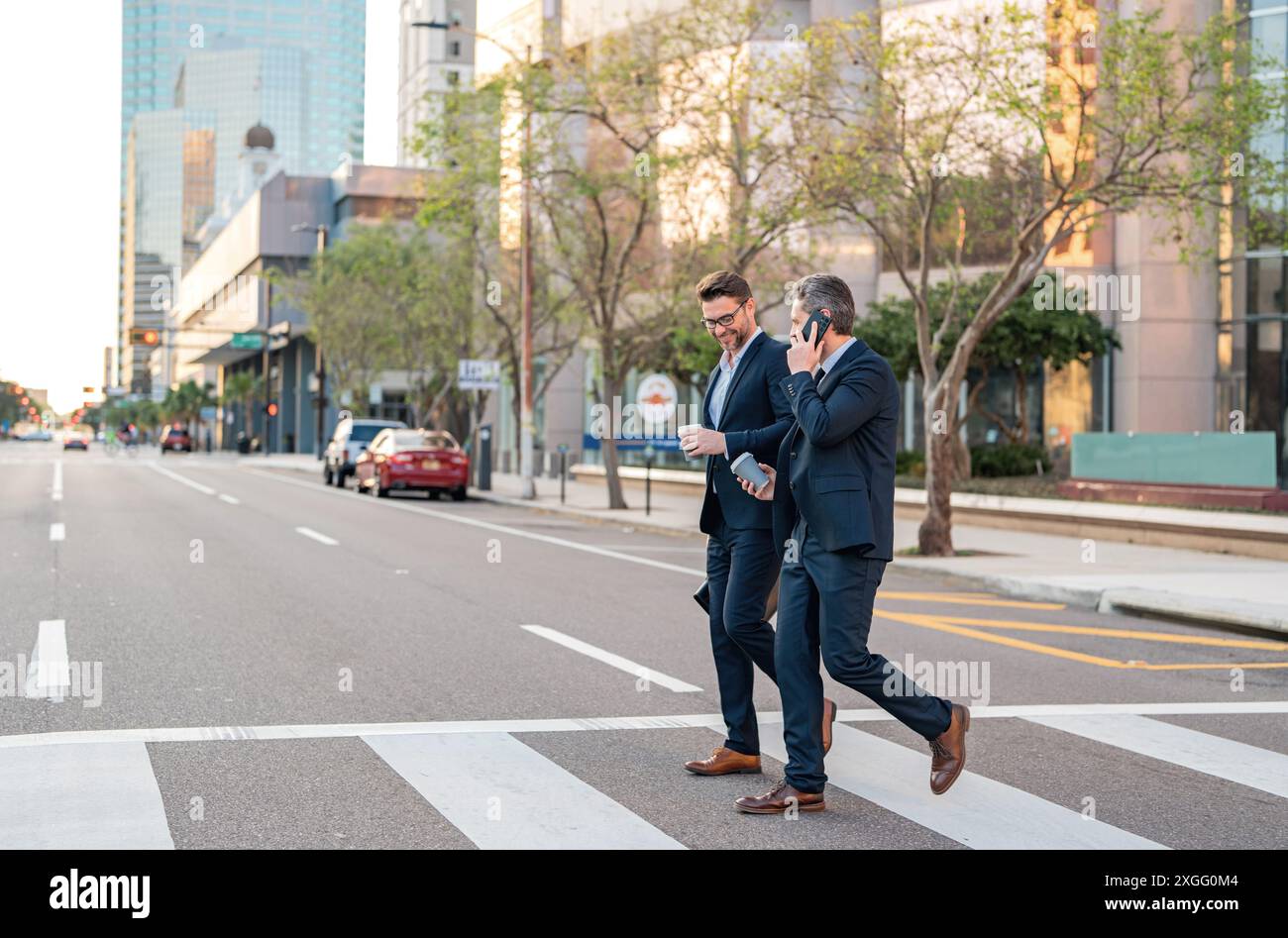 Photo of businessmen in suits walking outdoor through city street. Two ...