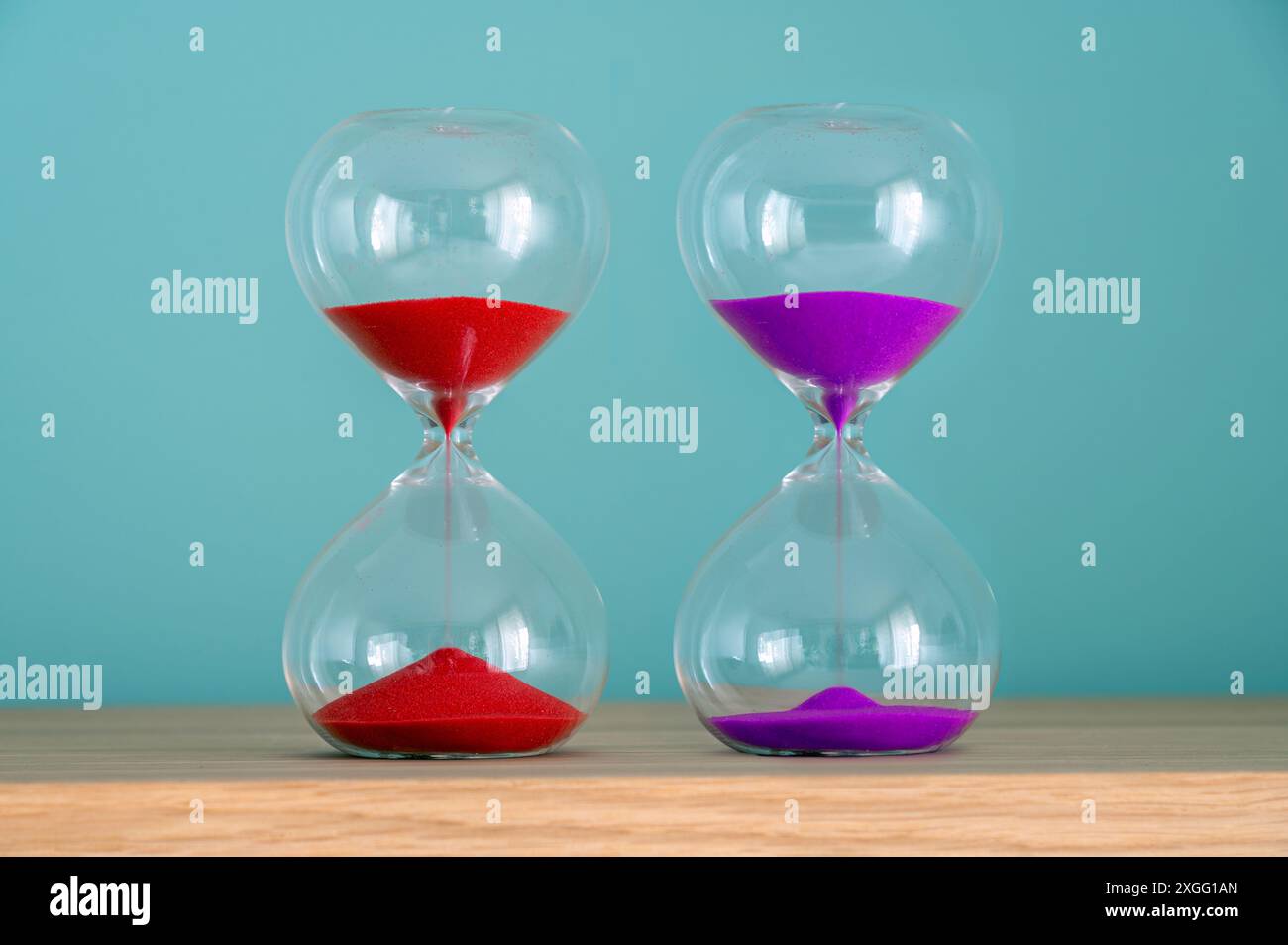 Two colorful hourglasses standing on a wooden surface are showing the ...
