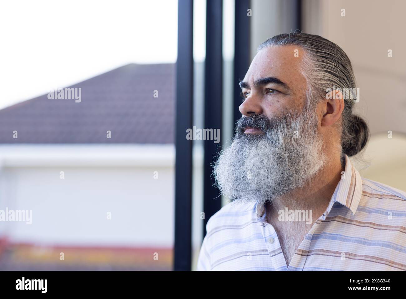 Pensive senior man with gray beard looking out window, contemplating ...