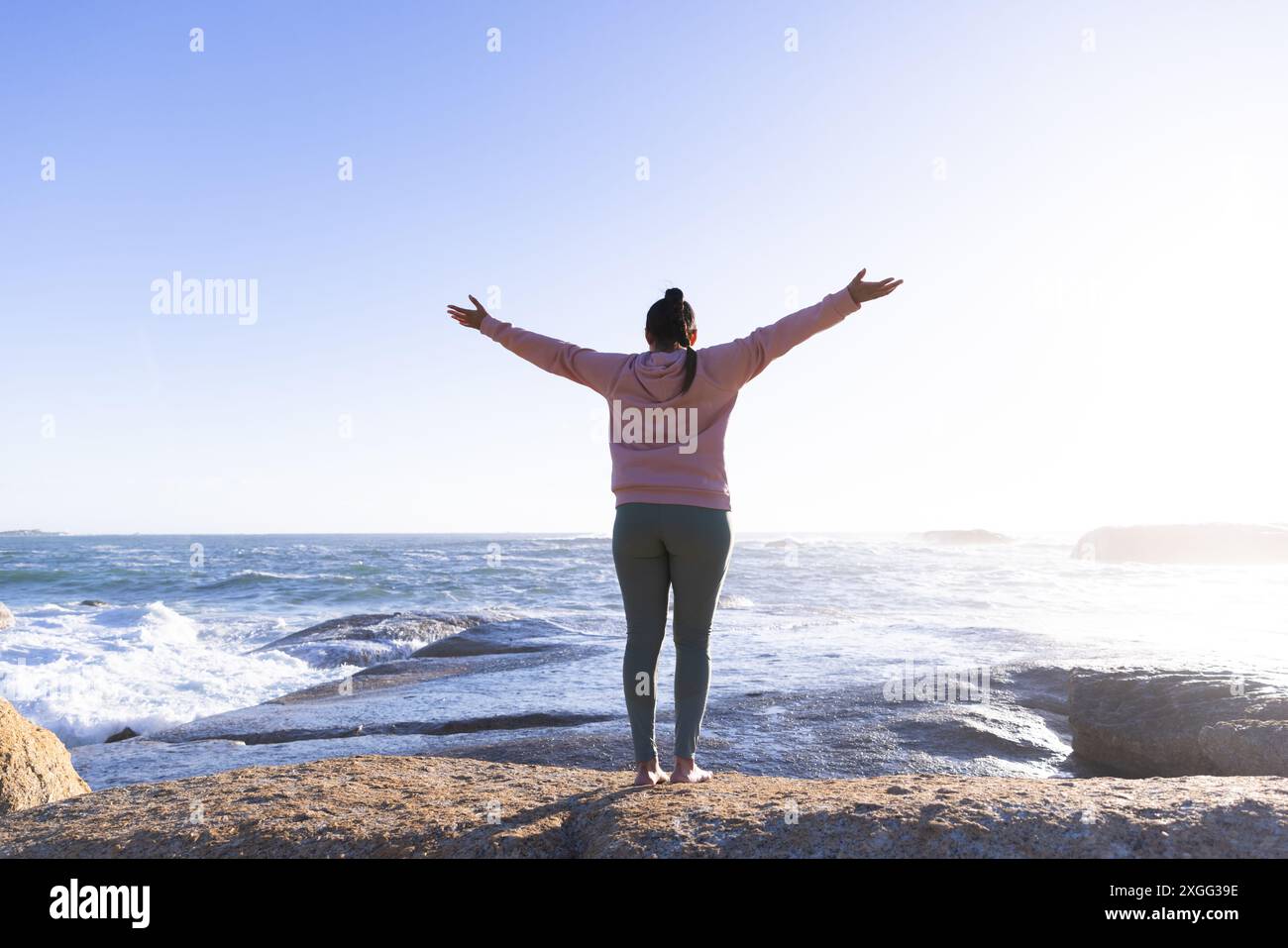 Standing on rocks by ocean, woman stretching arms and enjoying nature ...