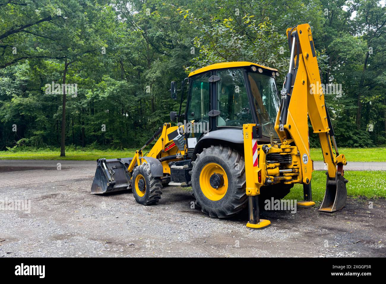 A yellow backhoe is parked on a gravel path in a forest setting. Its ...