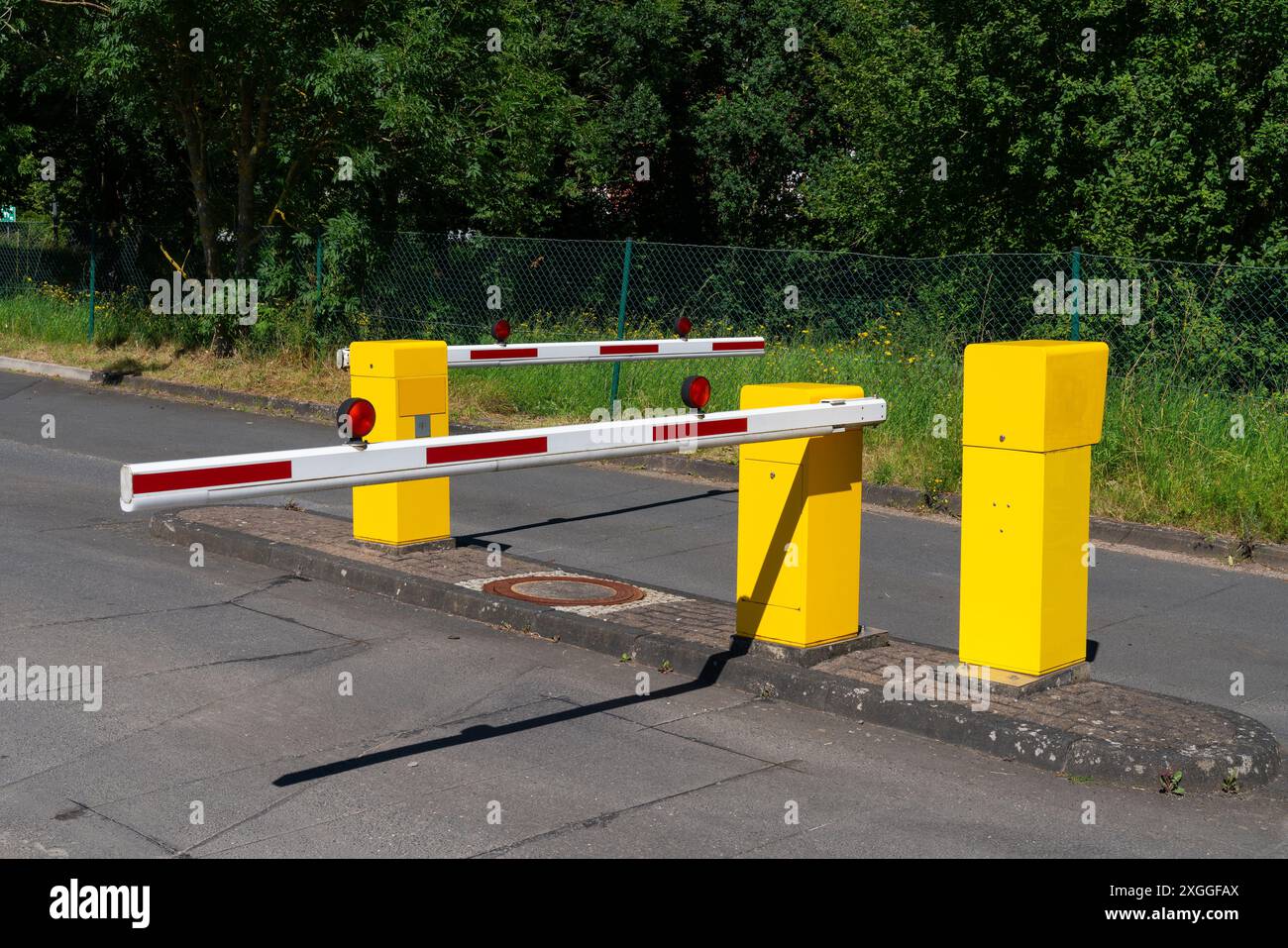 A closed gate barrier with red and white stripes, blocking a paved road ...