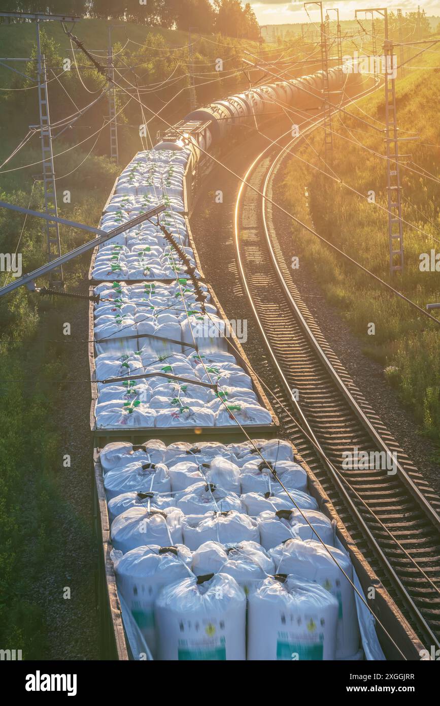 Freight train carrying cargo containers traveling on railway tracks during sunset, surrounded by ...