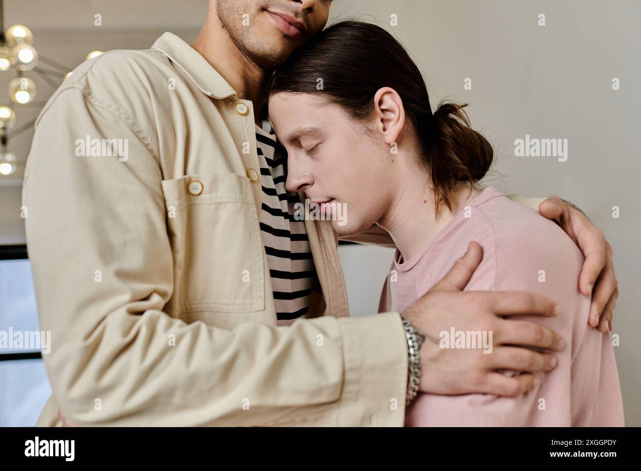 A young gay couple embraces in a modern apartment, showcasing a tender ...