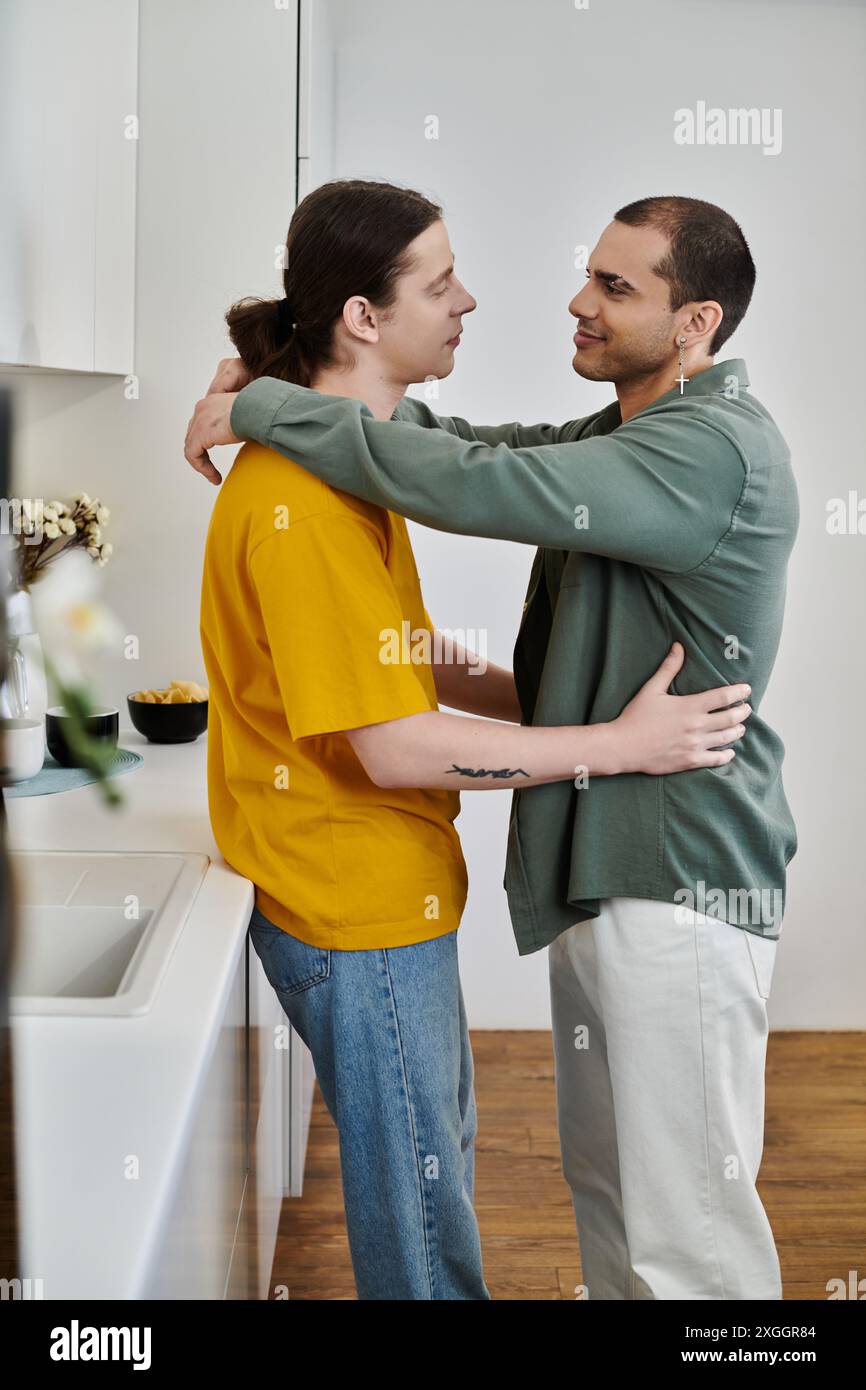 A young gay couple embraces in their modern kitchen, showcasing their ...