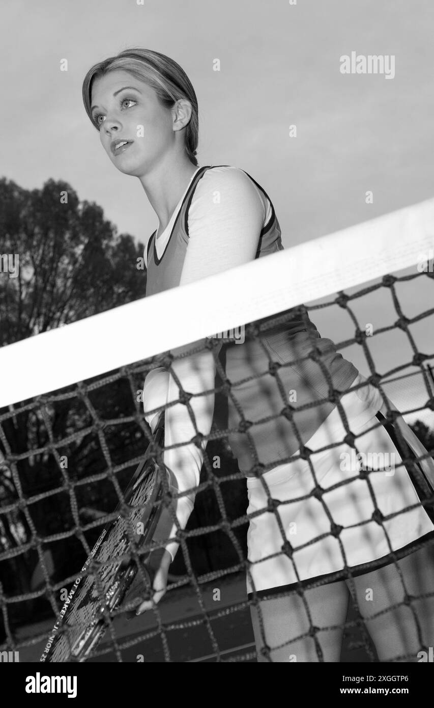 Teenage girl standing behind a tennis net, holding a racket, ready to ...