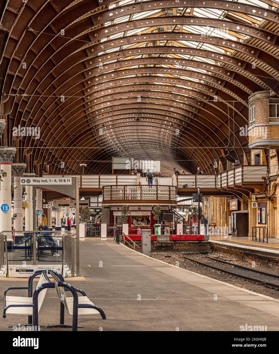 A railway station platform leads to a footbridge with a balcony. There ...