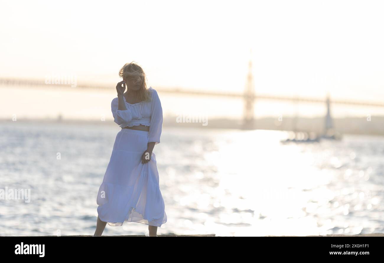 A woman in a white dress dancing on a dock overlooking a body of water ...