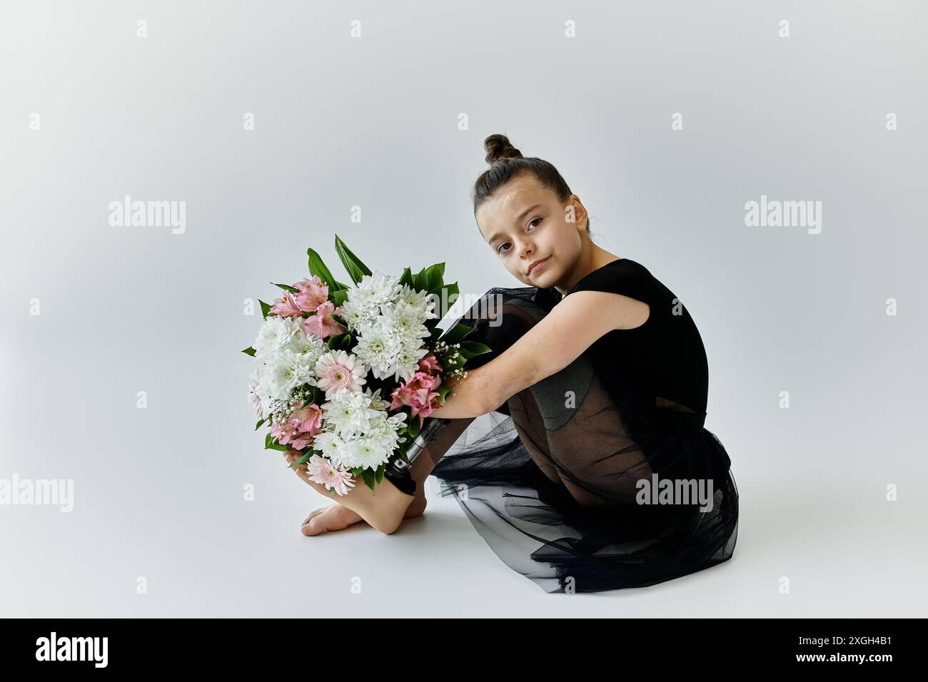 A young girl with a prosthetic leg, wearing a black leotard, sits with ...