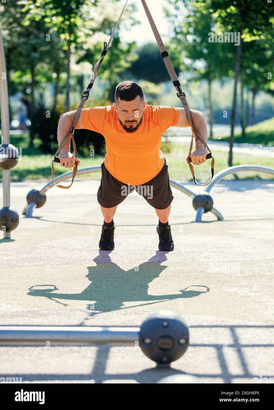 Bearded man in orange T-shirt and black shorts doing trx exercise with ...