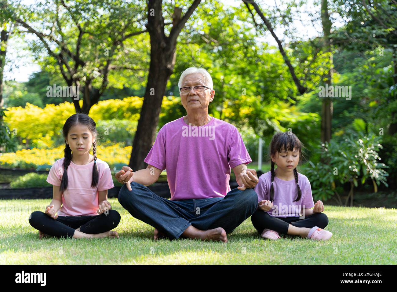 A grandfather and his two daughters sit on the grass in the sunshine ...