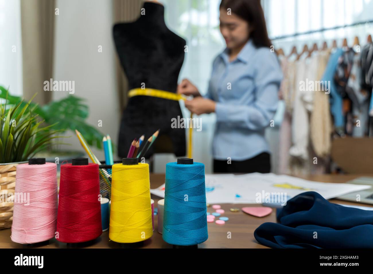 Beautiful young woman tailor holds fabric and thread at a tailor's shop ...
