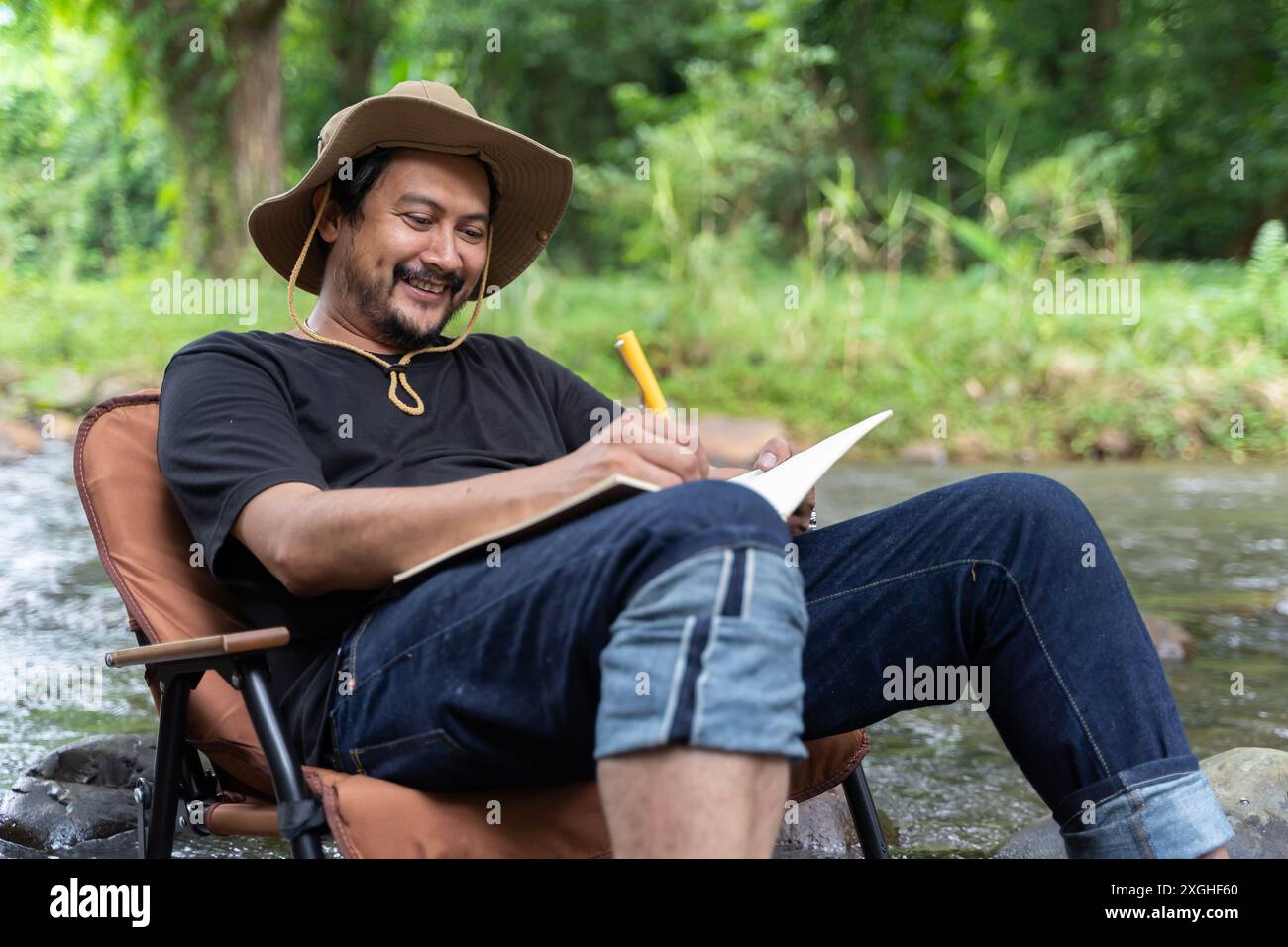 Handsome young man sitting in a chair immersed in water, writing, doing ...