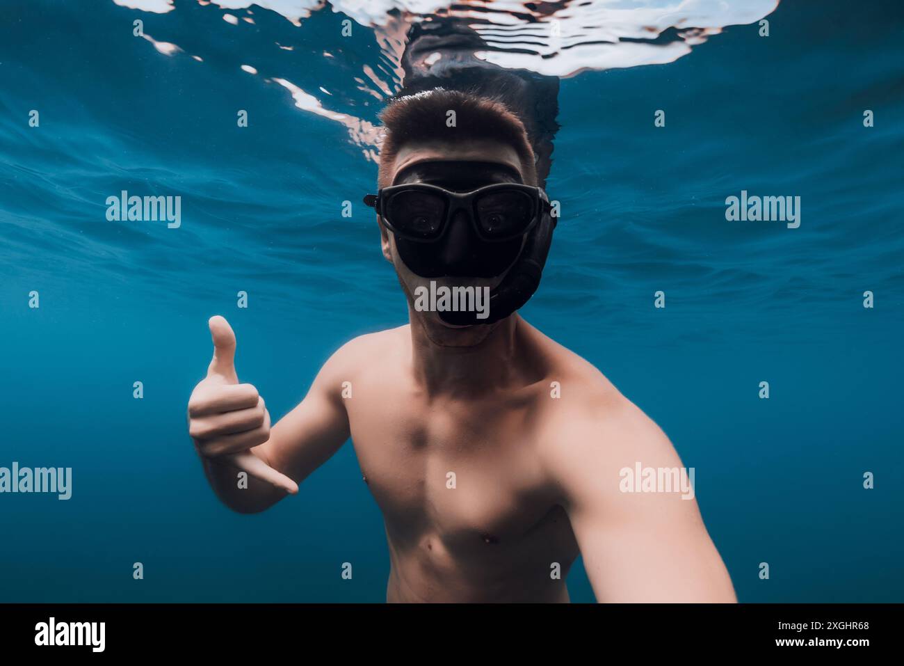 Man free diver in mask shows Shaka hand. Swimming underwater in blue ...