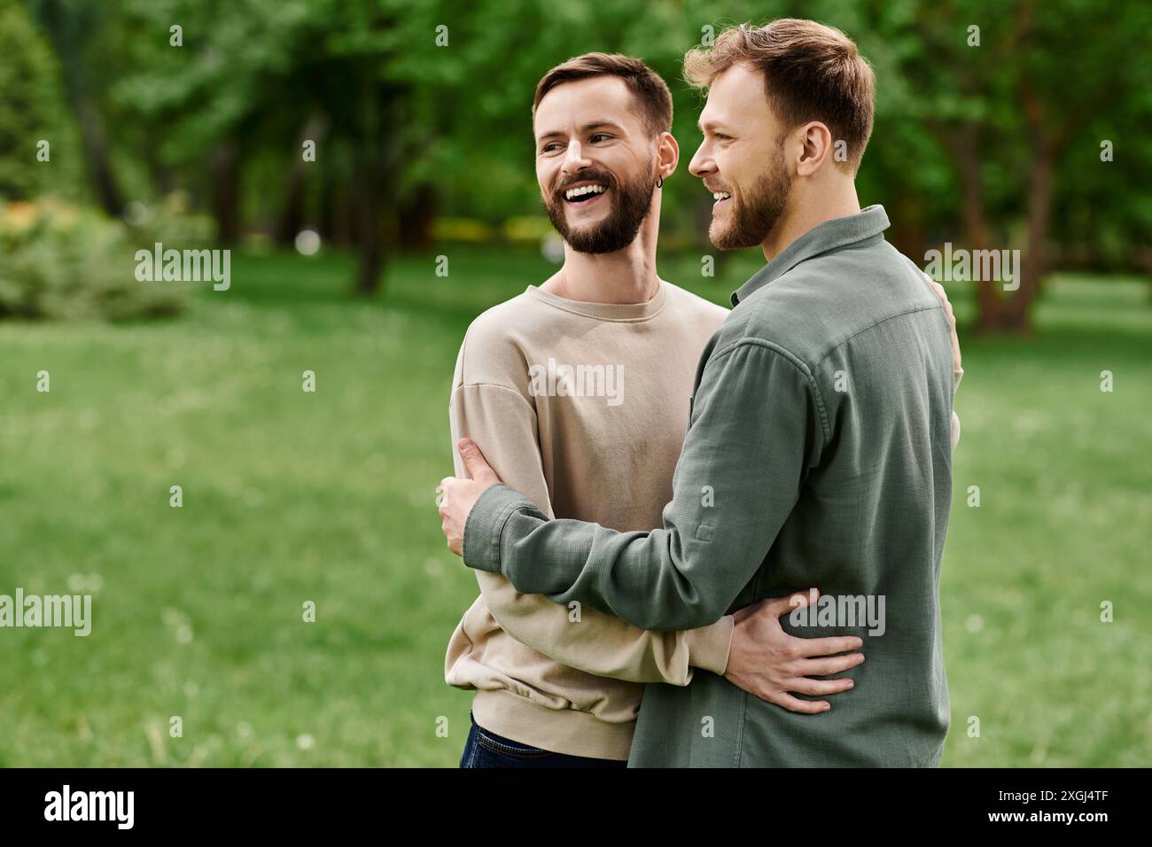 Two bearded men embrace each other while laughing in a grassy park ...
