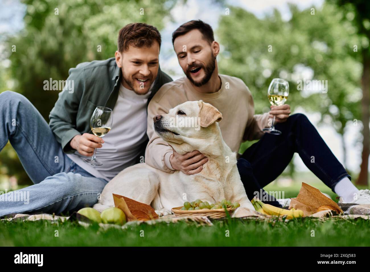 Two bearded men enjoy a picnic in a park with their labrador retriever ...