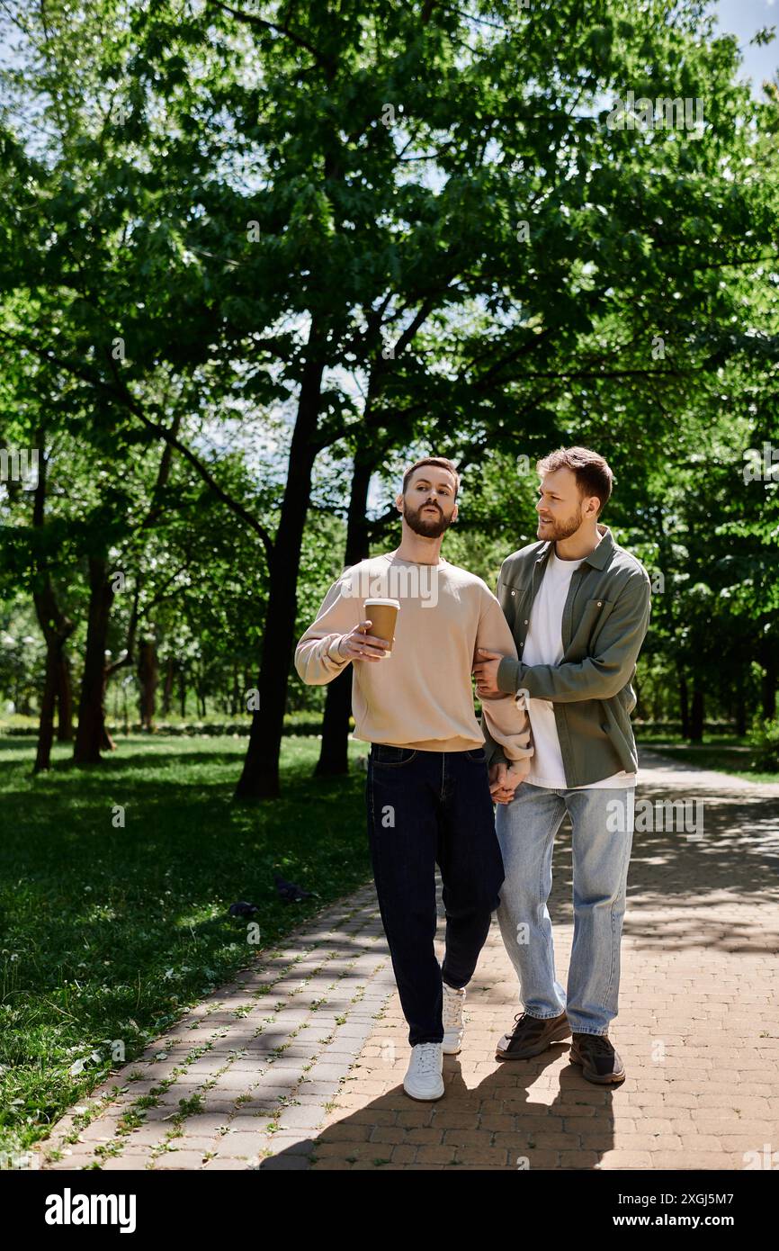 Two bearded gay men in casual attire hold hands and walk down a path in ...